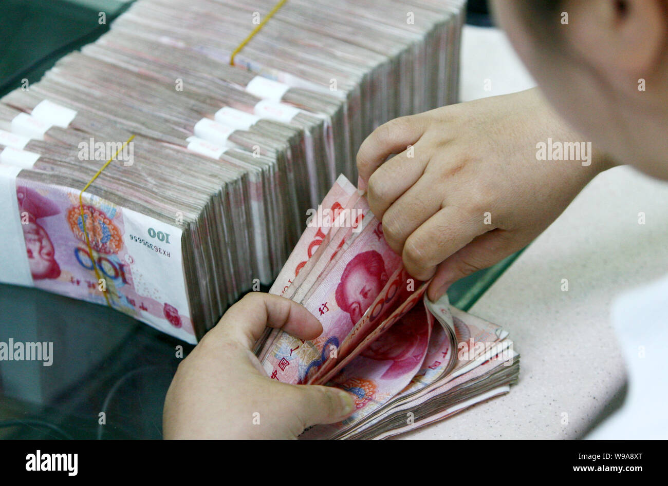 A Chinese clerk counts RMB (renminbi) yuan banknotes at a bank in ...