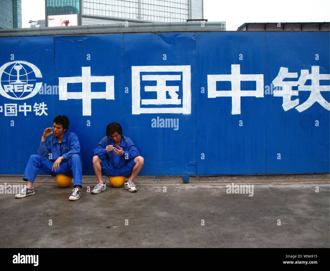 --FILE-- Two Chinese workers rest in front of an advertisement for ...