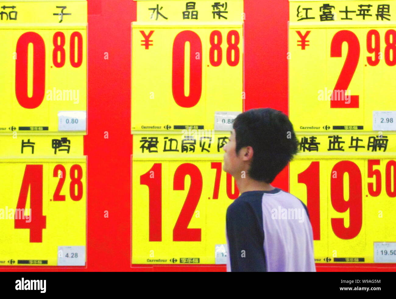 A Chinese man walks past some sign boards showing the price of fruits ...