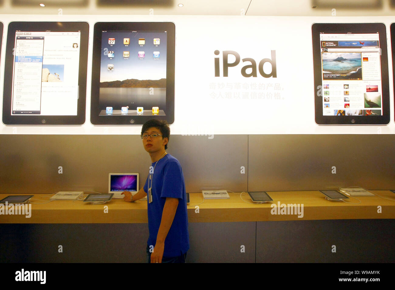 A Chinese employee stands in front of an advertisement for the iPad in ...