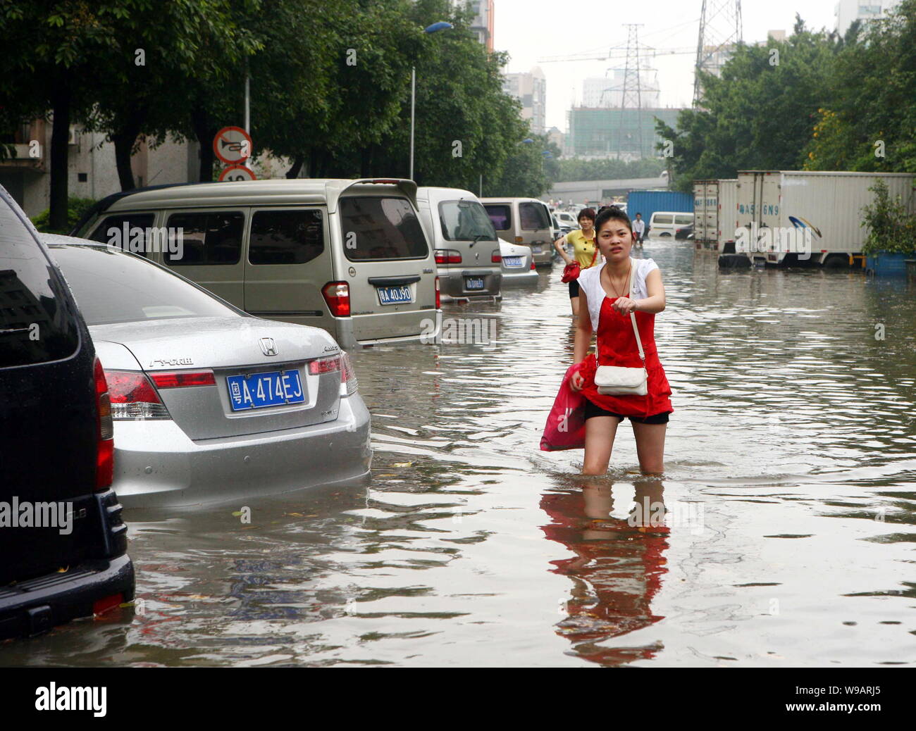 Local Chinese residents walk past cars on a flooded street after a ...