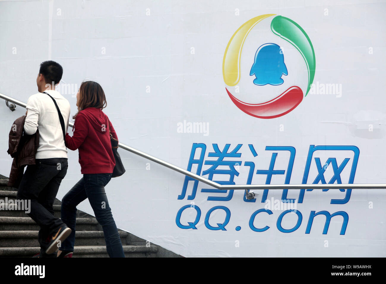 Local residents walk past an advertisement of QQ.com in Guangzhou city ...