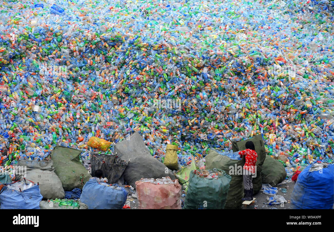 A Chinese worker labors in front of a big pile of waste plastic bottles ...