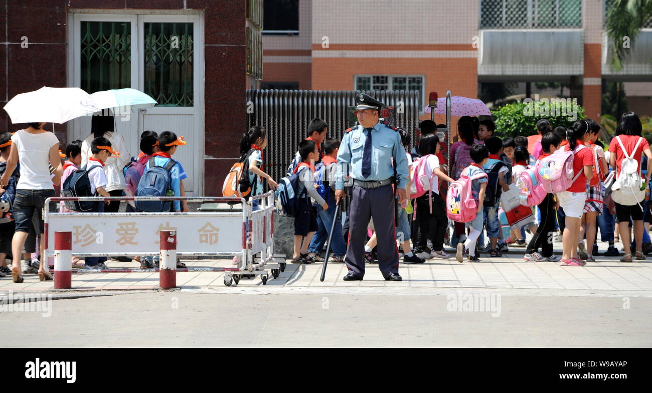 Chinese pupils walk past a security staff standing guard in front of ...
