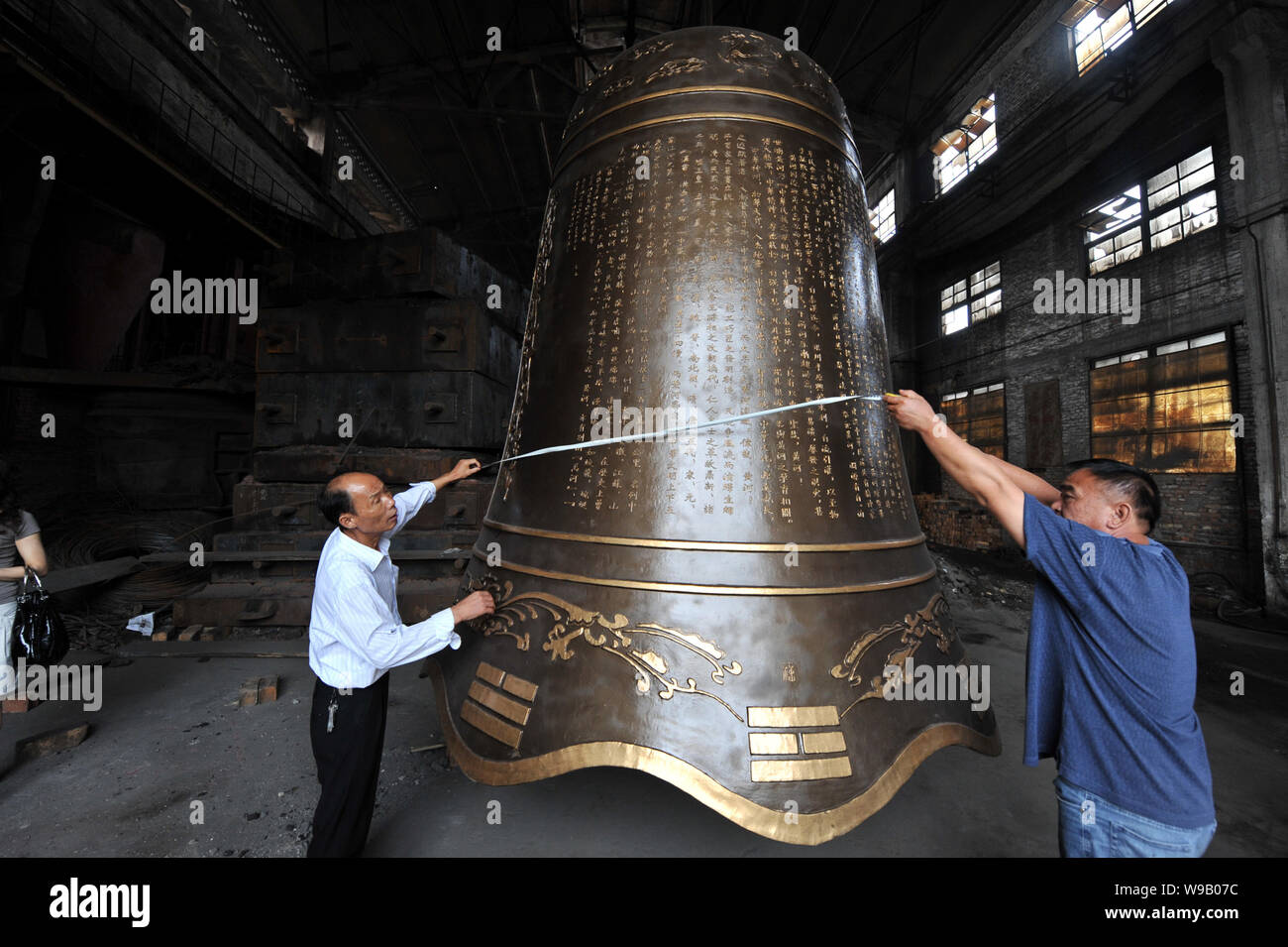 Chinese workers measures a bronze bell in a casting and forging plant ...