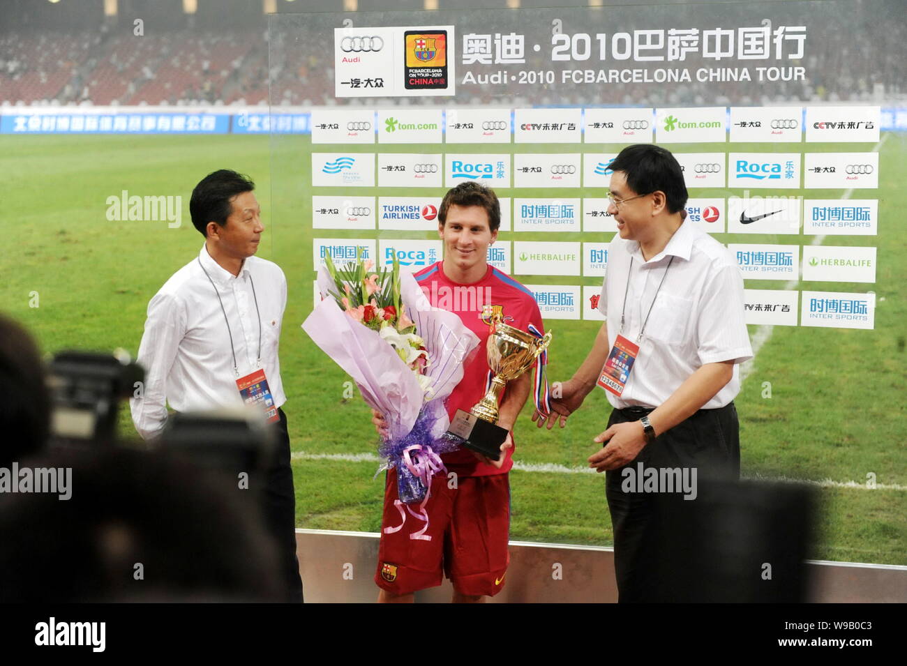 Lionel Messi of FC Barcelona holding flowers and a trophy poses next to ...