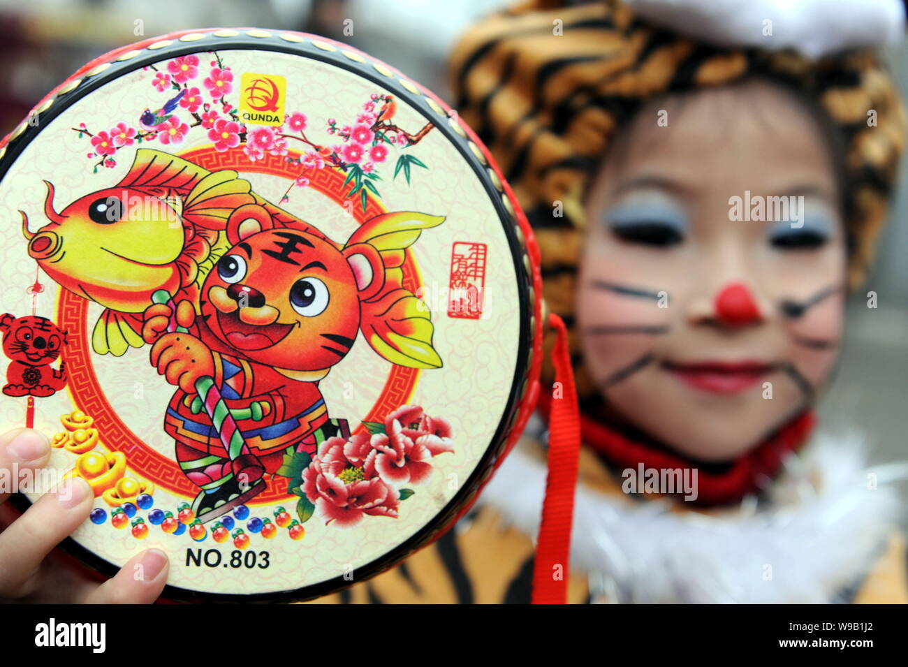 A Chinese girl dressed like the tiger shows a hand drum printed with a ...