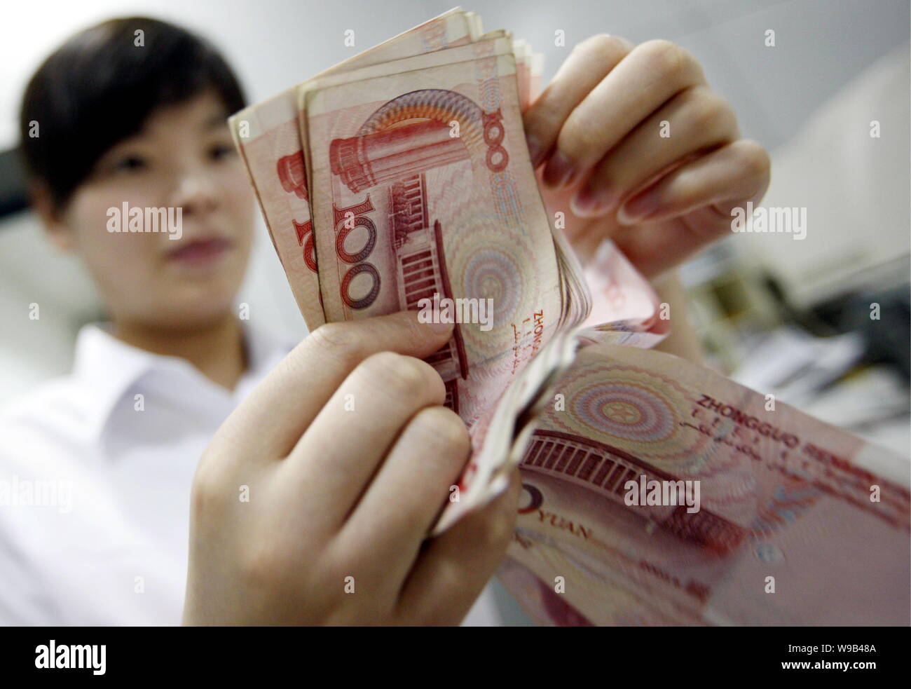 A Chinese bank clerk counts RMB (renminbi) yuan banknotes at a bank in ...