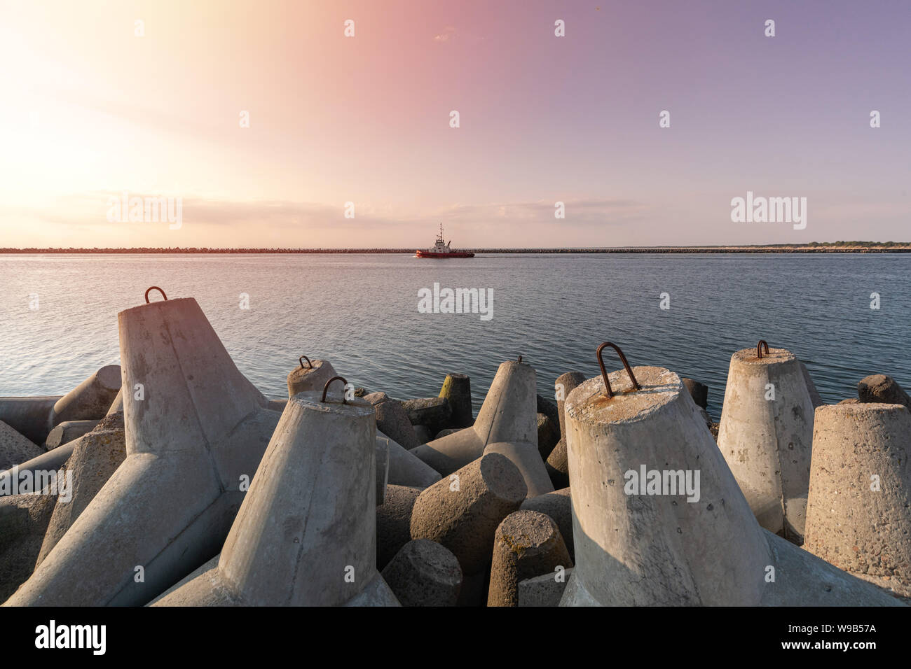 Tugboat sailing in sea to tow ship to port. Tetrapod breakwaters in ...
