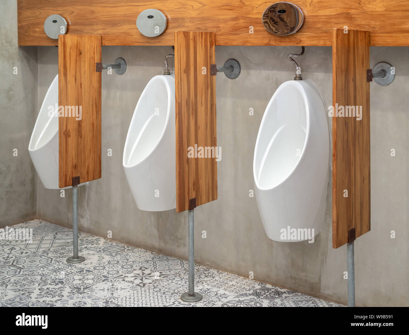 Three modern white automatic urinal for men and wood partitions on ...