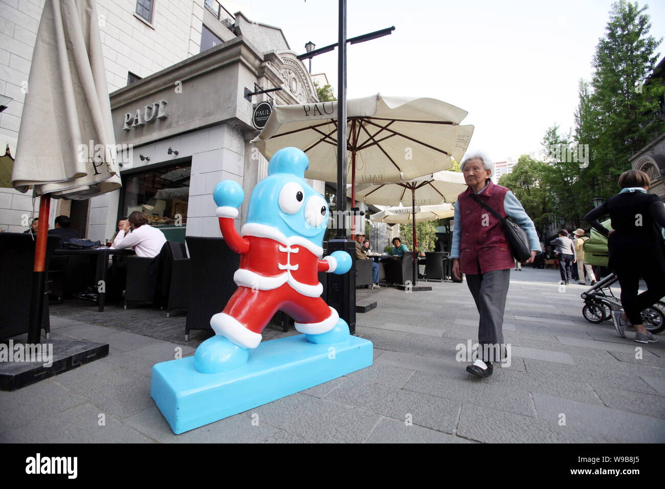 An elderly woman walks past a Haibao figure, the official mascot of the ...