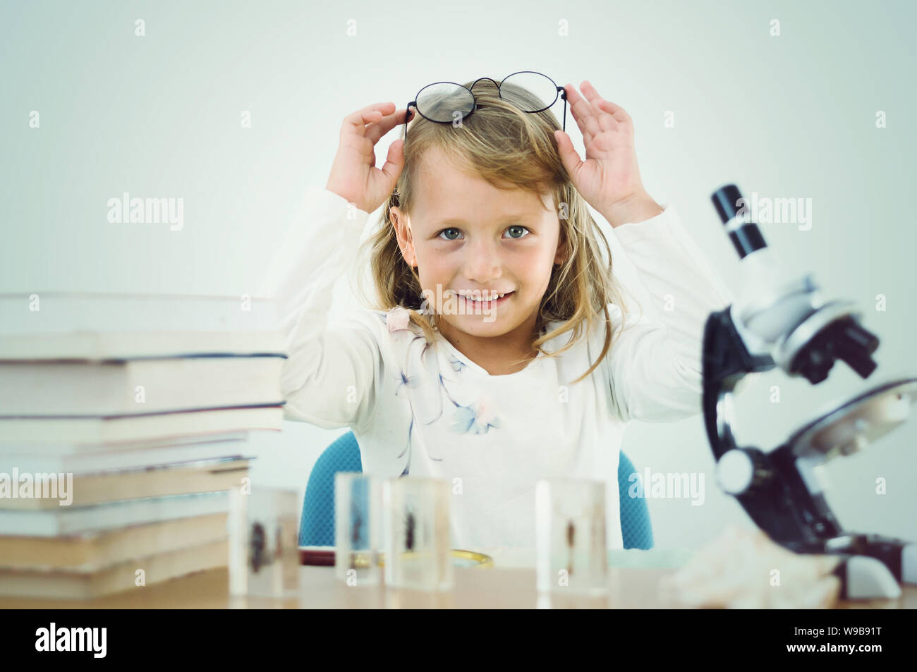 little girl playing scientist among stacks of books with a microscope ...