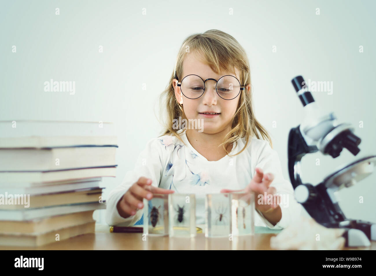 little girl playing scientist among stacks of books with a microscope ...