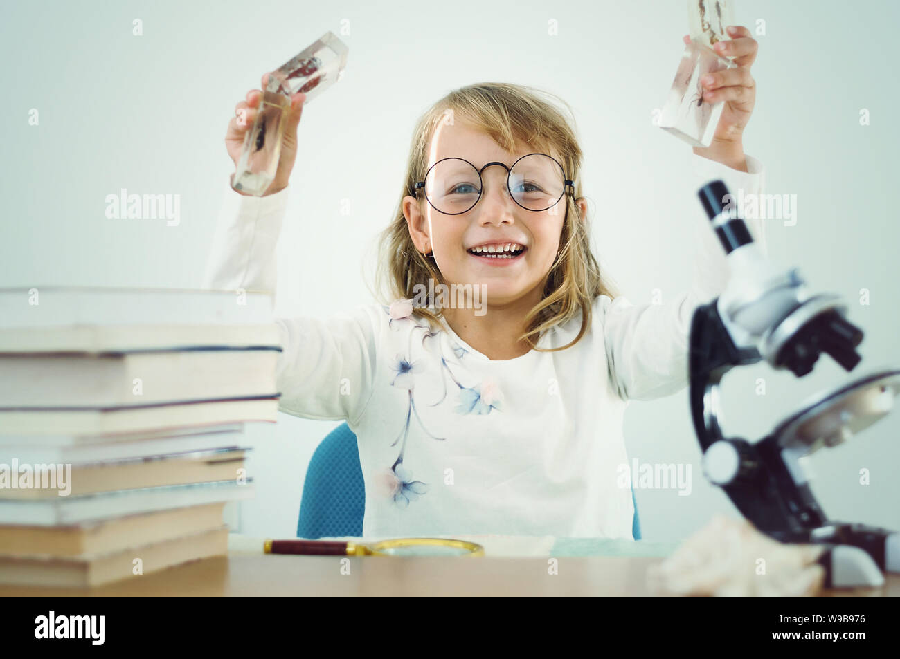 little girl playing scientist among stacks of books with a microscope ...
