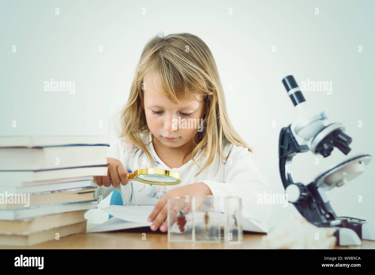 little girl playing scientist among stacks of books with a microscope ...