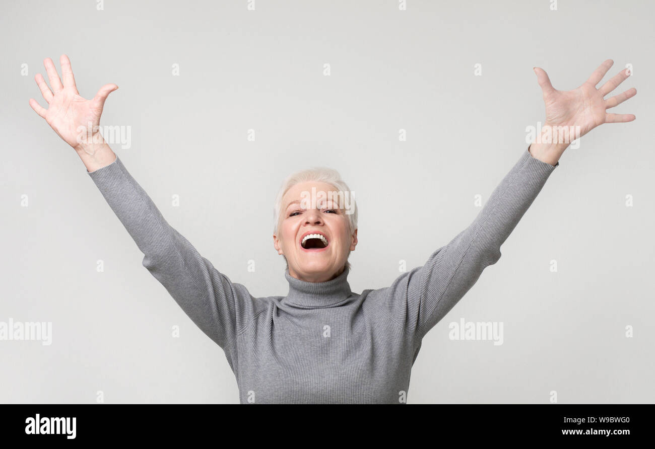 Excited senior woman rejoice success exclaiming on light studio ...