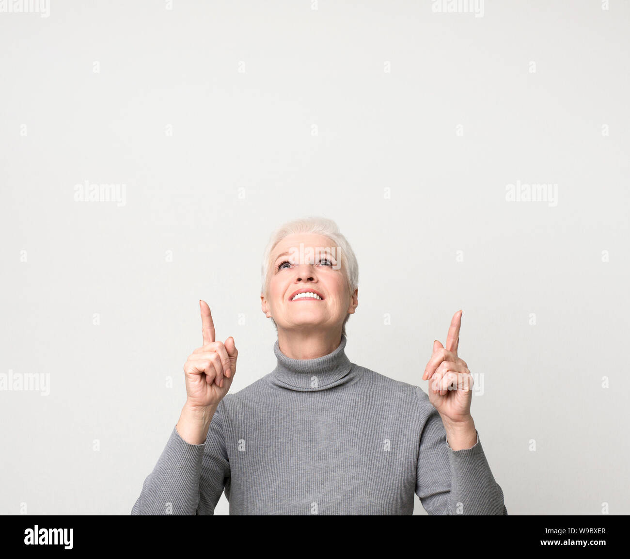 Great offer. Beautiful senior woman pointing upwards at copy space ...
