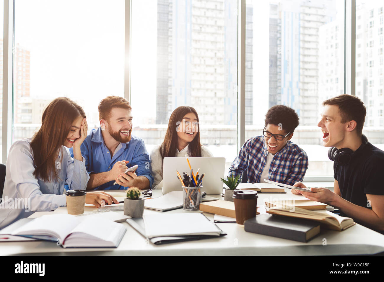 University students sitting together at table with books and laptop ...