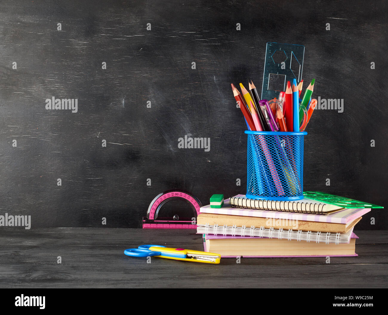 stack of notebooks, blue glass with multi-colored wooden pencils and ...