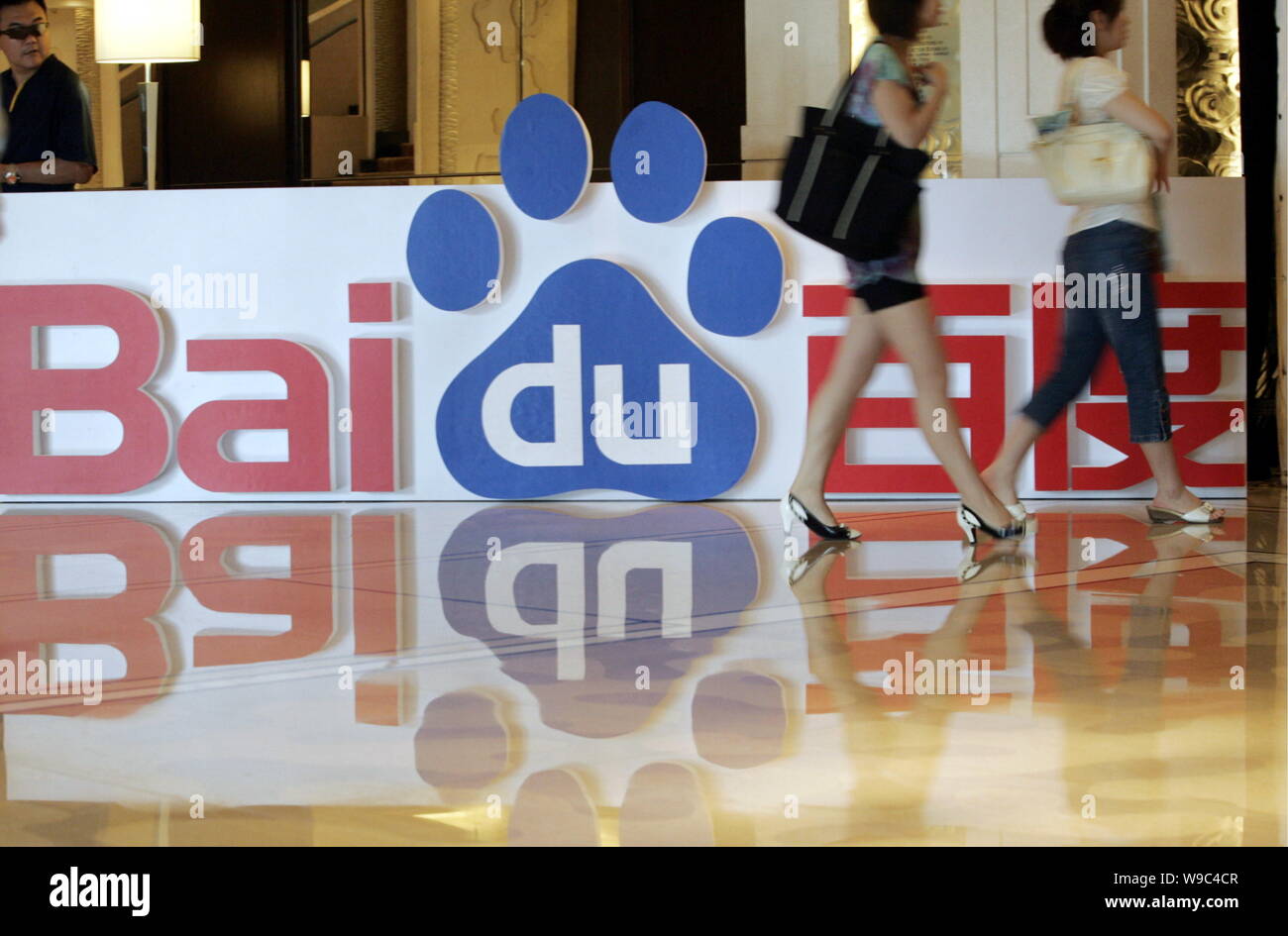 Young Chinese women walk past the logo of Baidu during a press ...