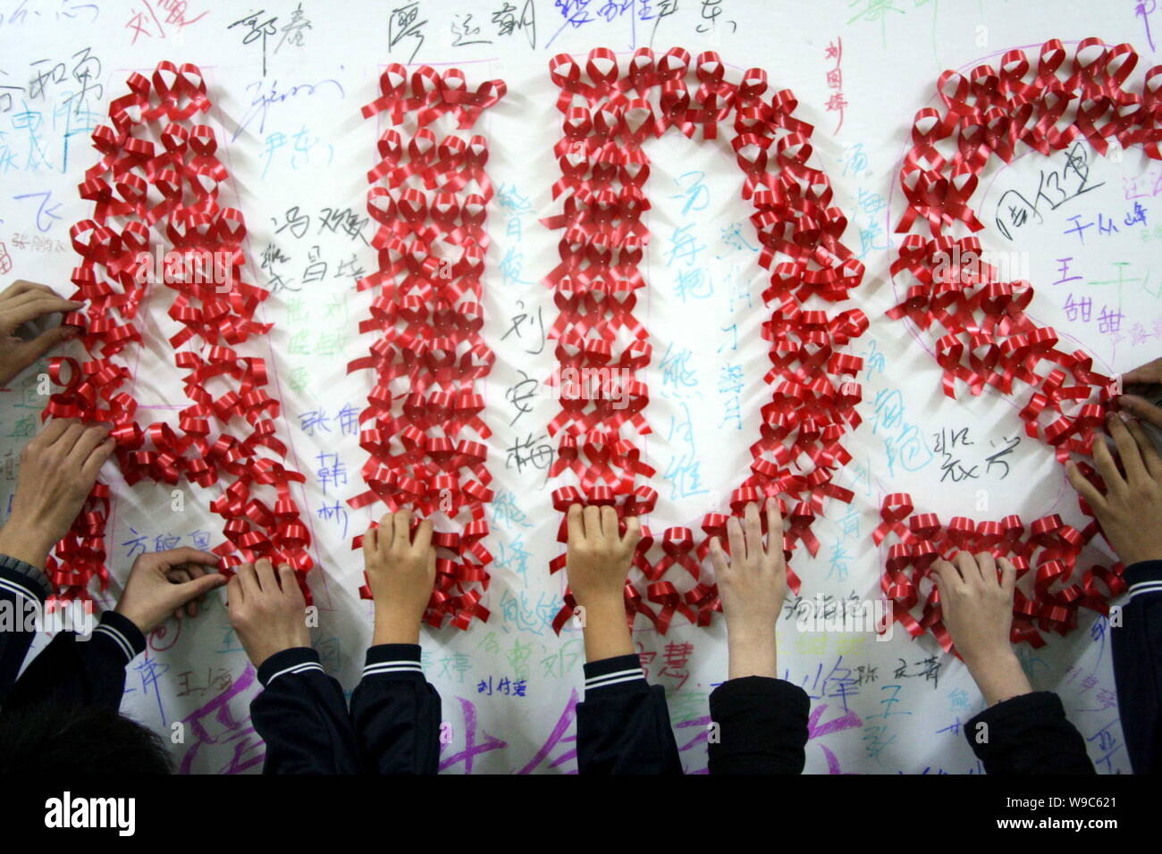Chinese students make the sign of AIDS with red ribbons at a middle ...