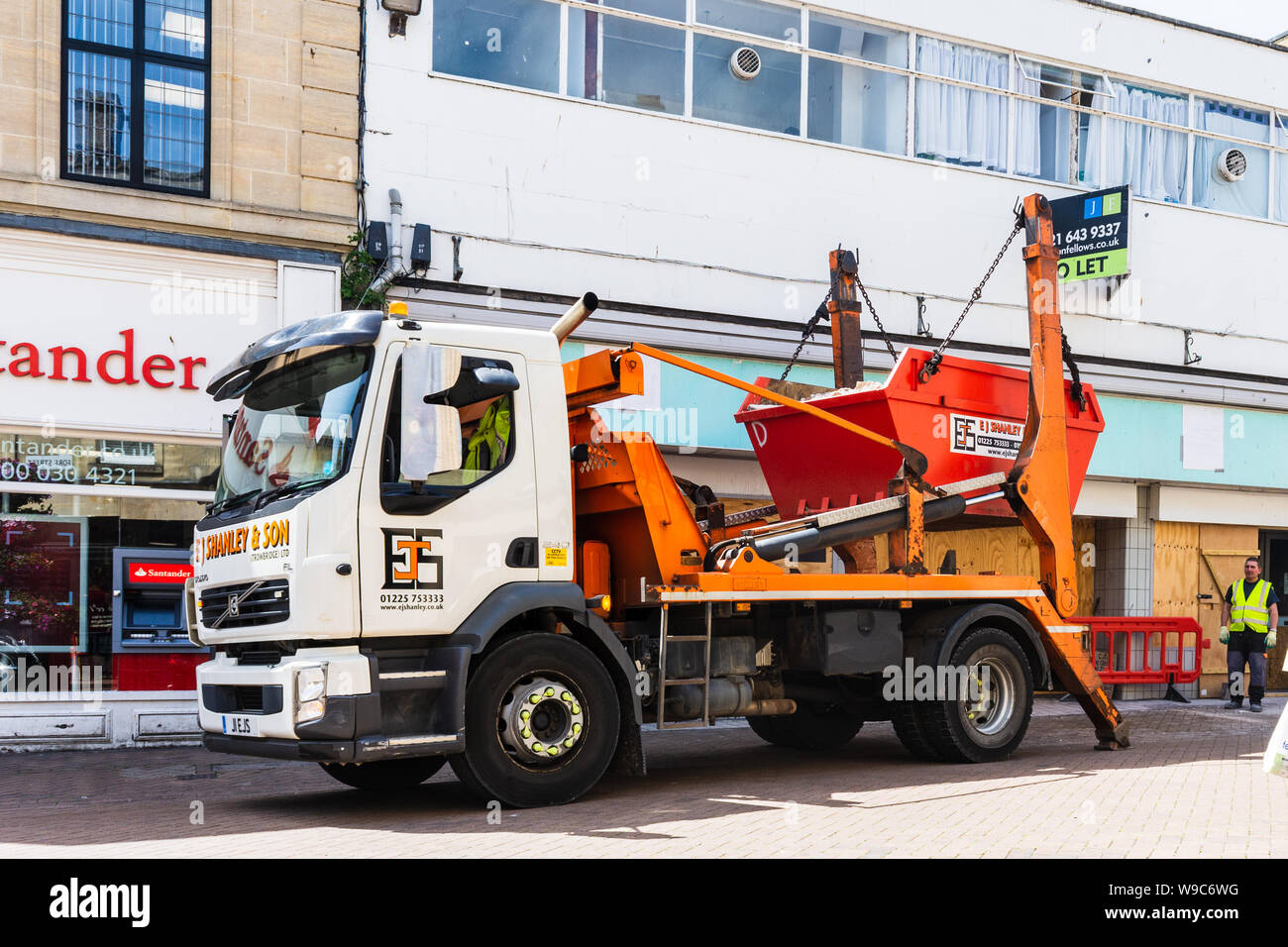 A skip lorry by a shop under refurbishment, with the driver using ...