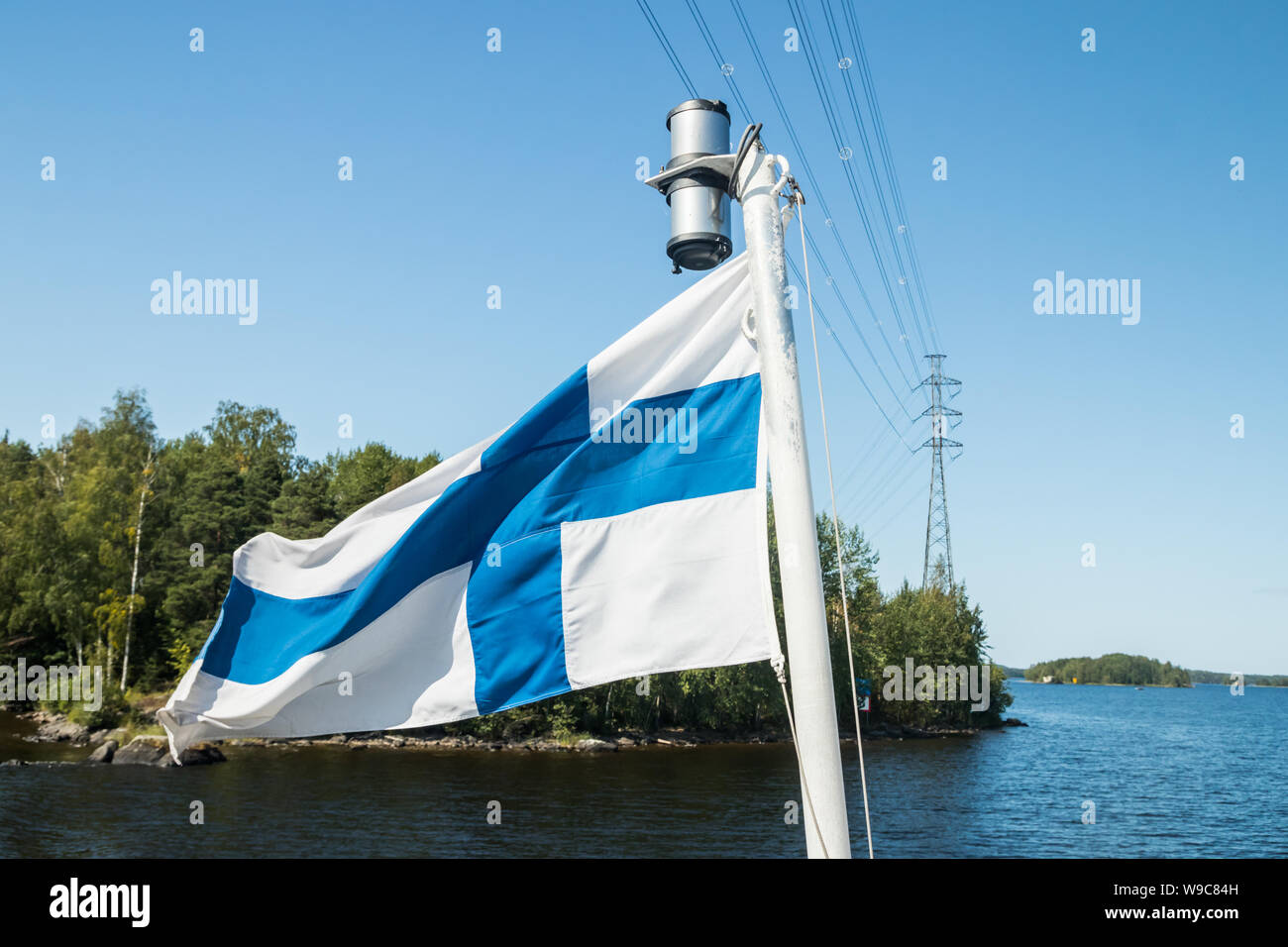 A finnish flag on a boat in the wind and high voltage line on lake ...