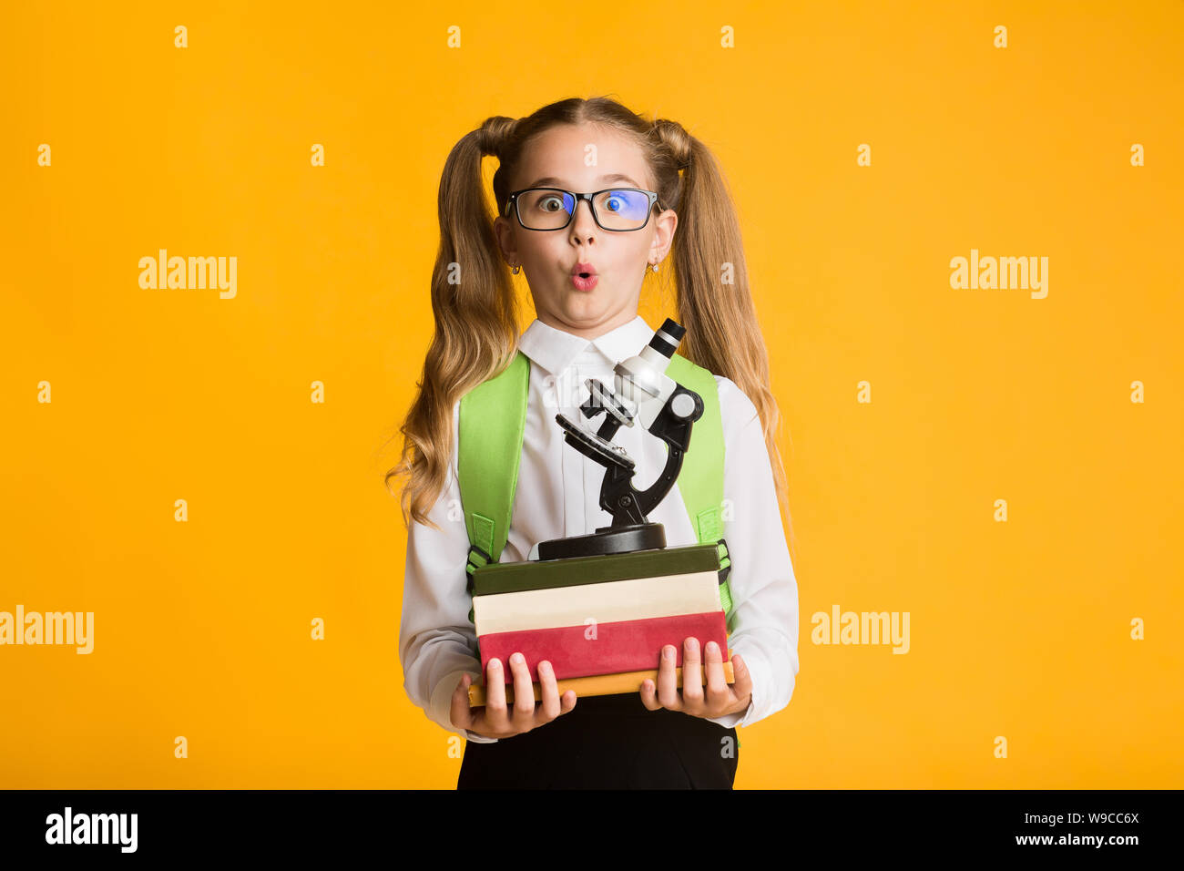 Funny First-Grade Schoolgirl Holding Stack Of Books And Microscope ...