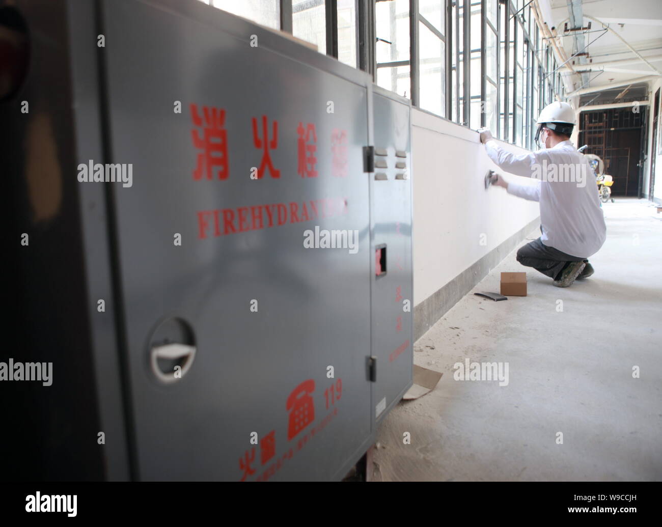 A Chinese worker polishes the wall near a fire hydrant case in a ...