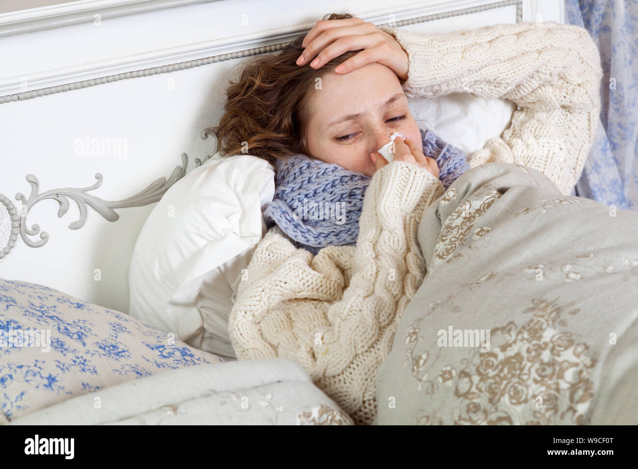 Sad alone young woman in white sweater and blue scarf feeling cold sick ...