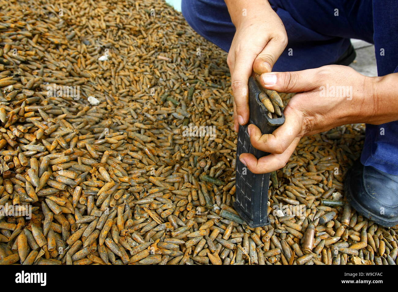 A Chinese man loads a cartridge clip with bullets next to a pile of ...