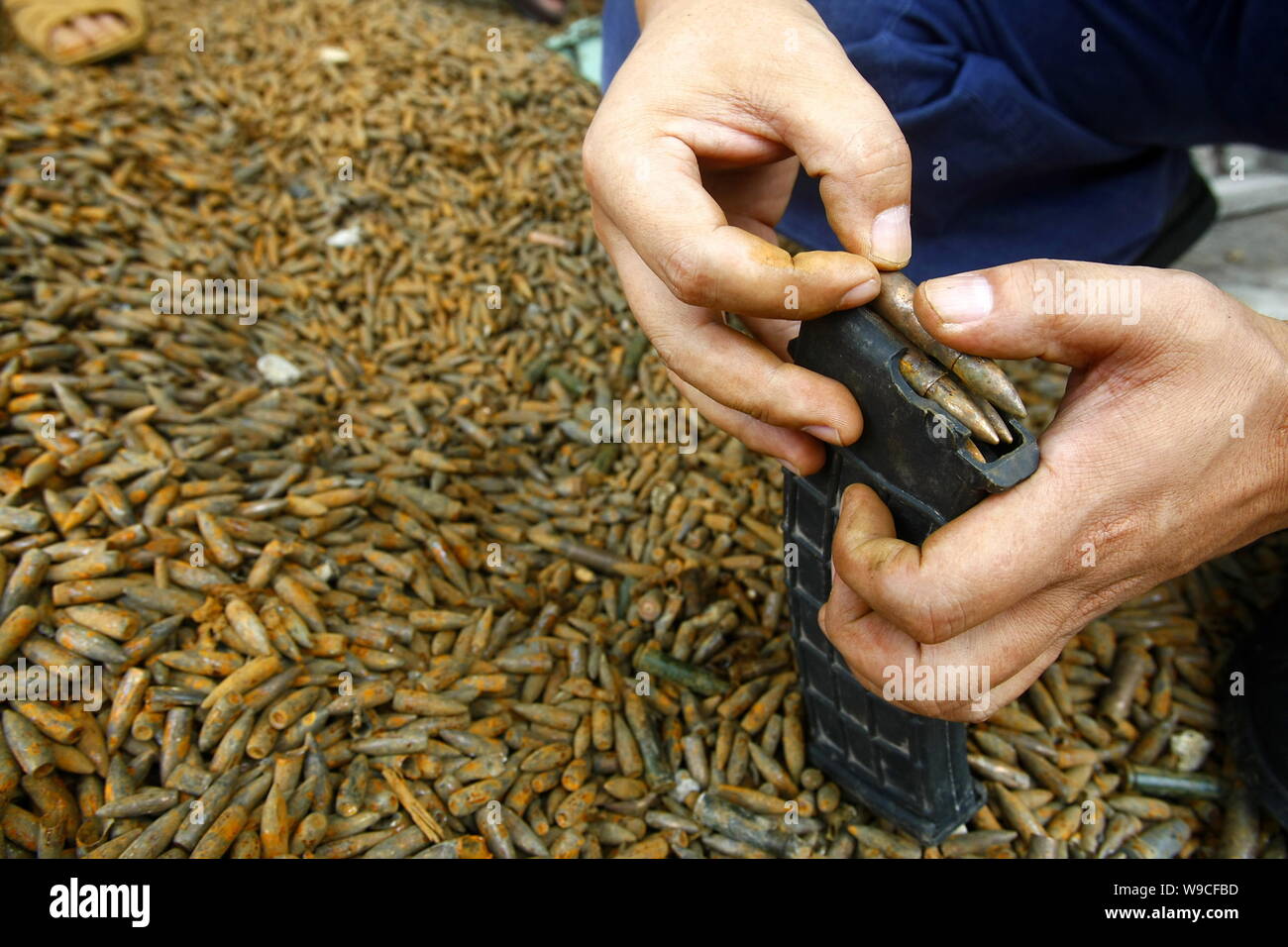 A Chinese man loads a cartridge clip with bullets next to a pile of ...