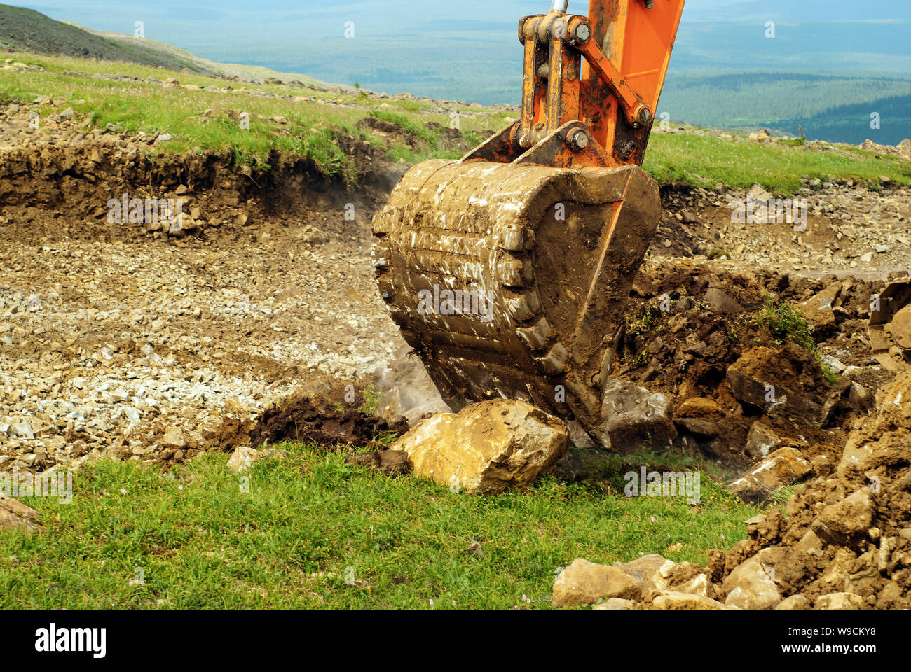 bucket of a working excavator tears off the grass and soil cover ...