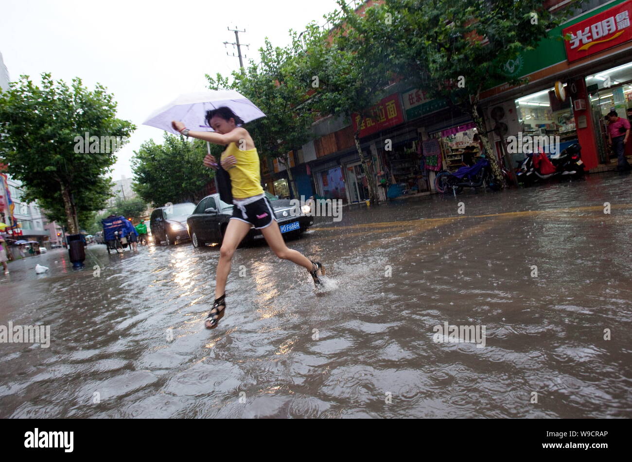 A young Chinese woman runs across a flooded street after heavy rain in ...