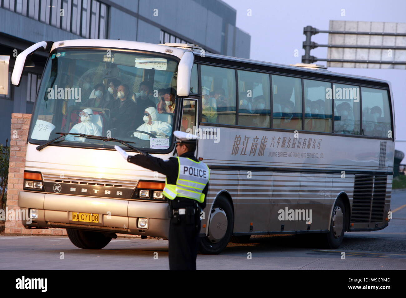 A Chinese police officer directs a bus carrying masked Chinese ...