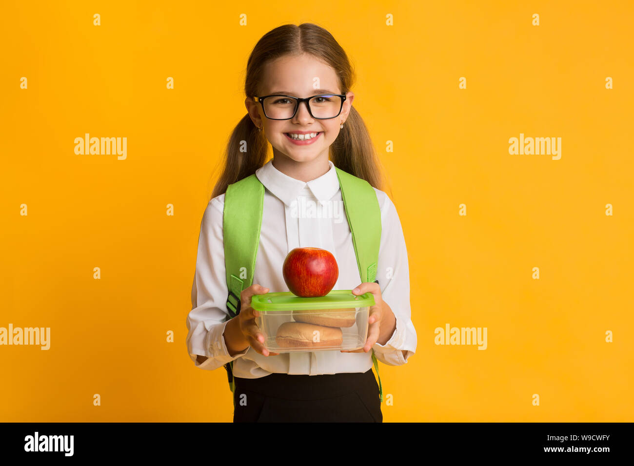 Cute Schoolgirl Holding Lunch Box Over Yellow Studio Background Stock ...