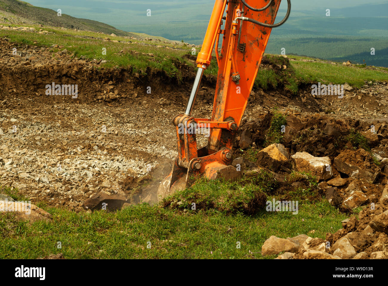 bucket of a working excavator tears off the grass and soil cover ...