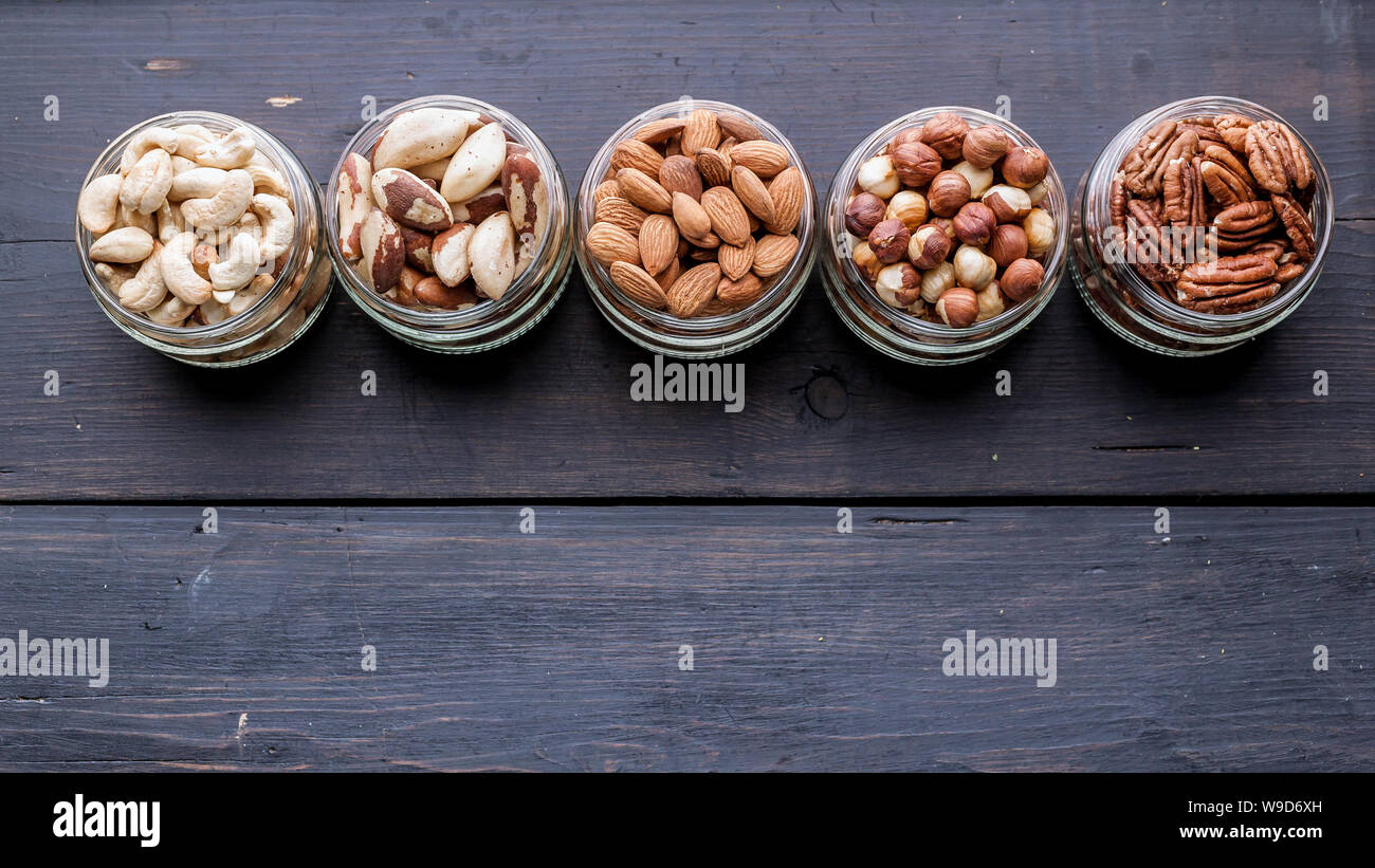 Different kinds of nuts in jars on a dark wooden background. Copy space ...