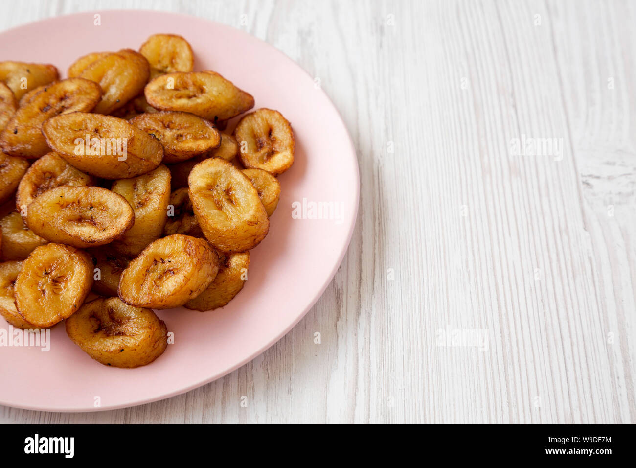 Homemade fried plantains on a pink plate on a white wooden background ...