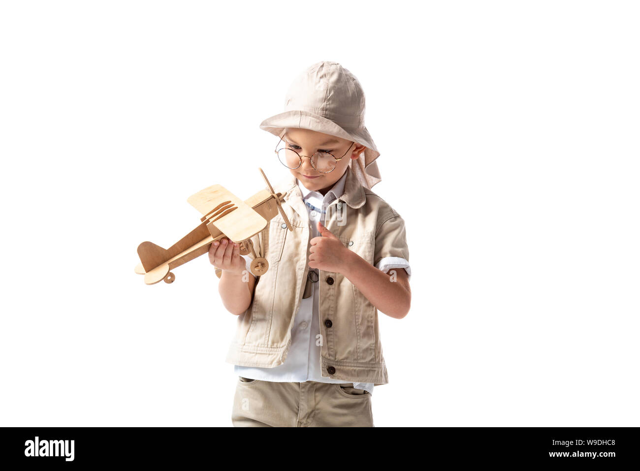 dreamy explorer boy in glasses and hat holding wooden toy plane ...