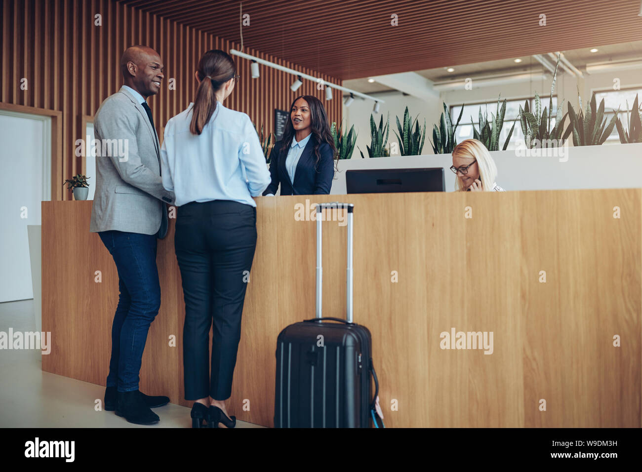 Two smiling guests talking with a concierge while checking in together ...
