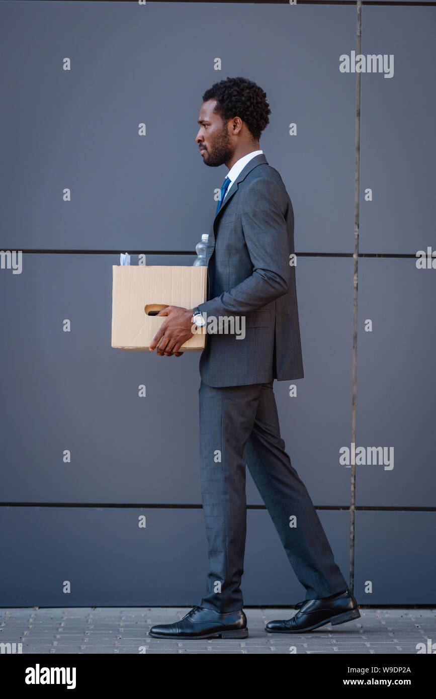 side view of fired african american businessman holding carton box ...