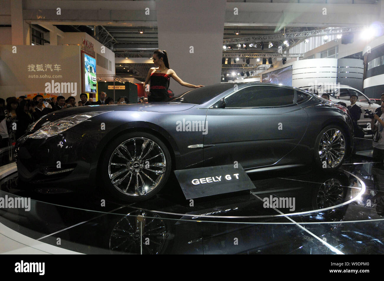 Visitors look at a model posing with a Geely GT concept roadster during ...