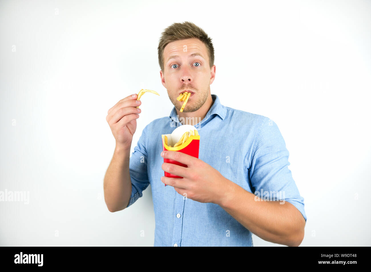 funny young man standing with french fries in his mouth on isolated ...