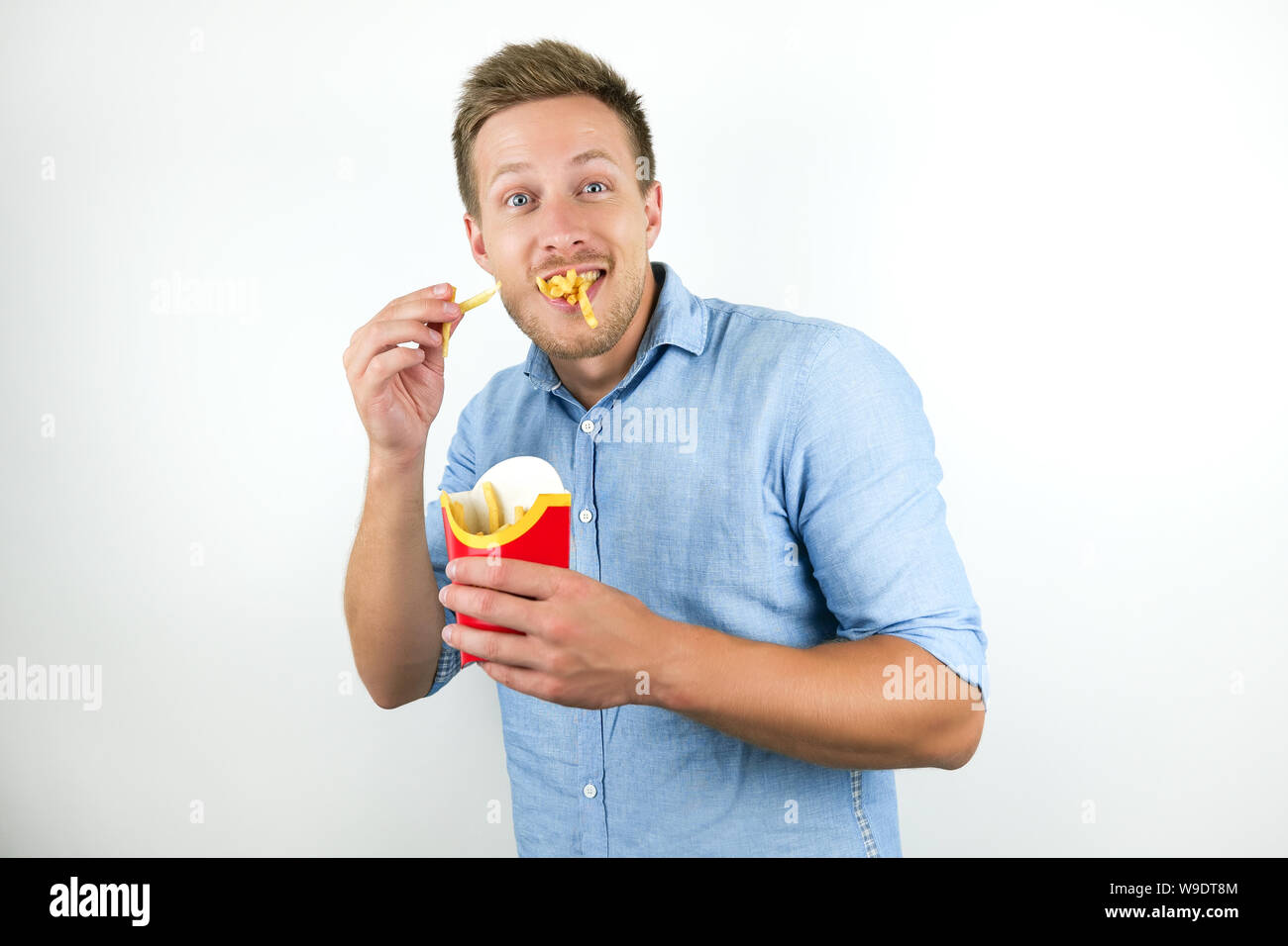 young handsome man eats french fries from fast food restaurant looks ...