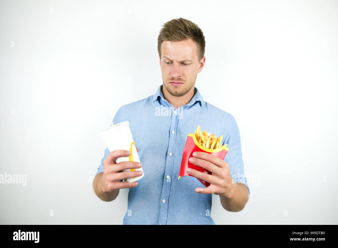 young handsome man looks at fast food french fries and soda drink with ...