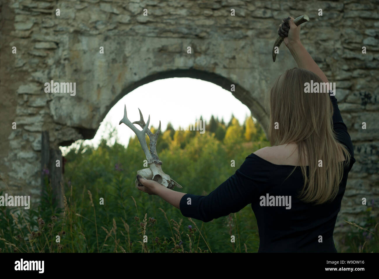 witch - young woman in black dress conducts some sinister pagan rite ...