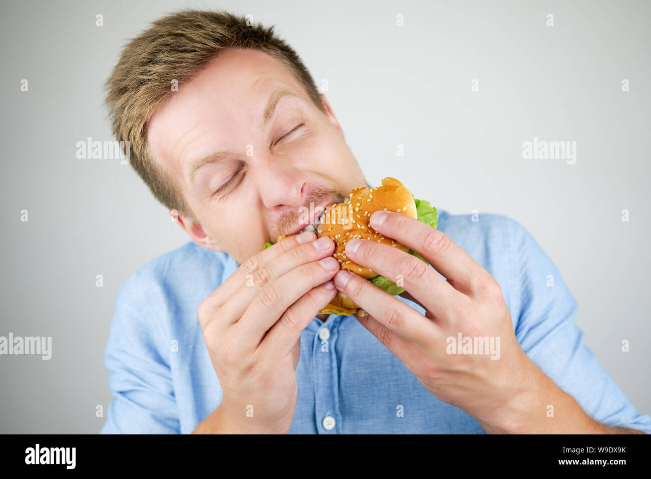 young handsome man biting fresh tasty burger from fast food restaurant ...