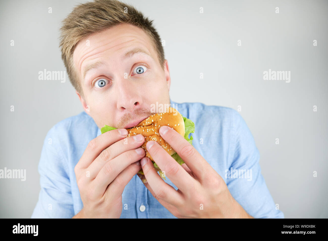 young handsome man biting burger from fast food restaurant looks hungry ...