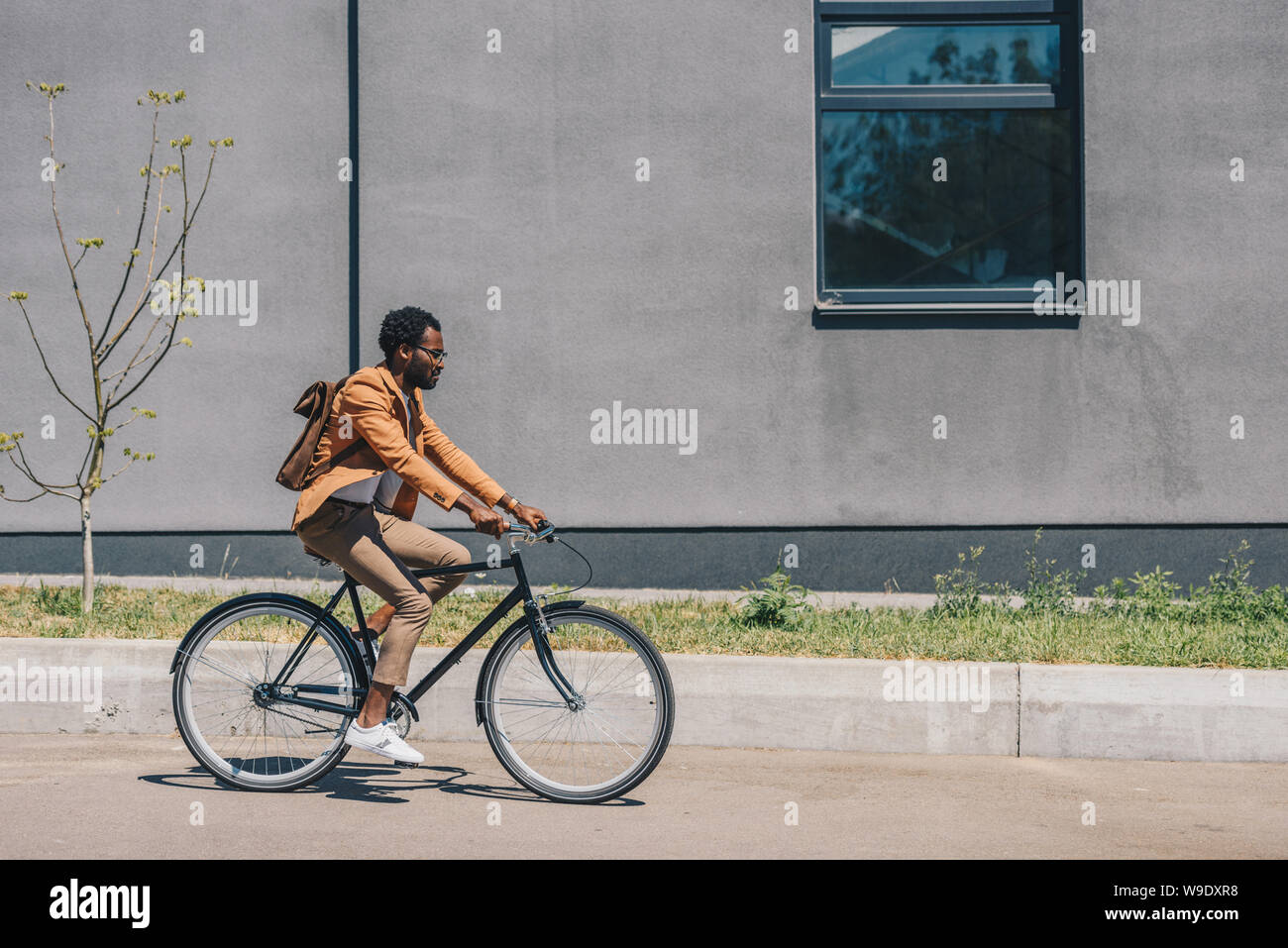 stylish african american businessman riding bicycle on sunny street ...